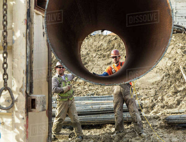 Caucasian workers hauling pipe at construction site - Royalty-free ...