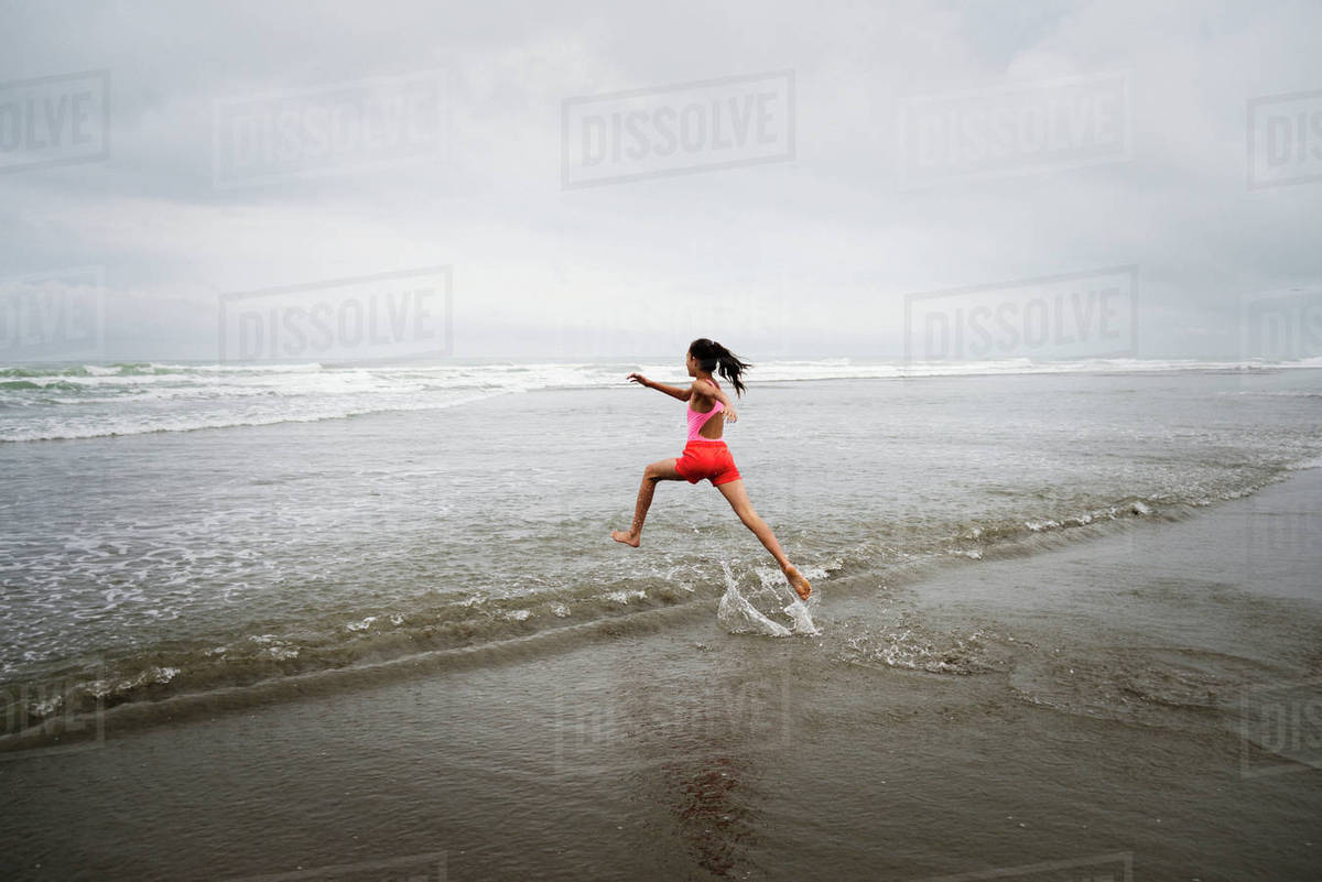 Mixed race girl running into ocean on beach - Stock Photo - Dissolve