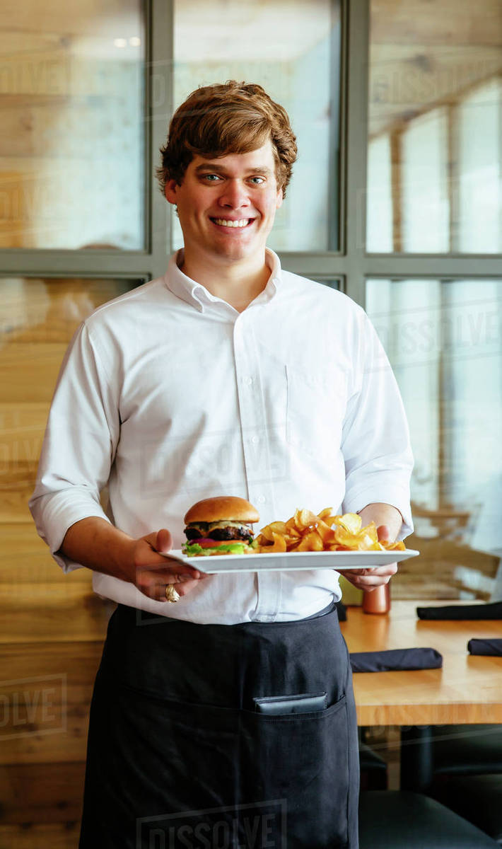 Caucasian waiter carrying cheeseburger and chips in cafe - Royalty-free ...