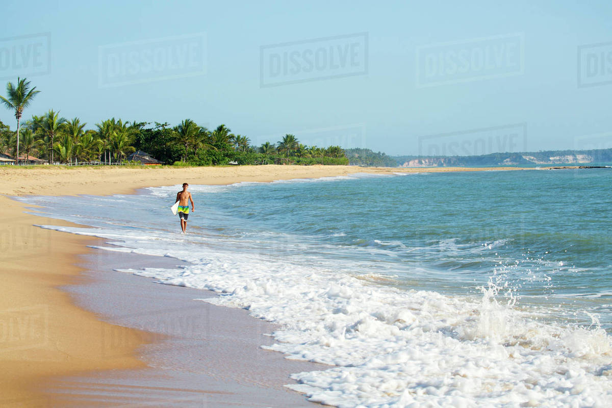 Mixed race surfer carrying surfboard on beach - Stock Photo - Dissolve