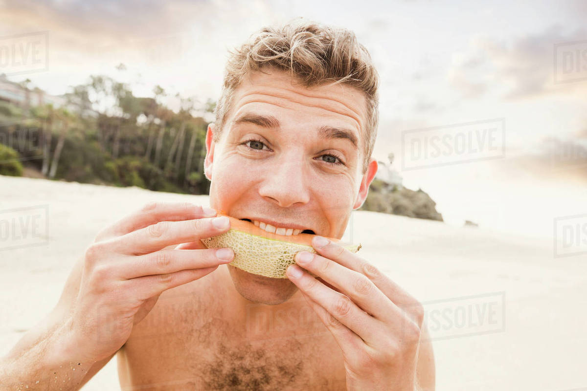 Caucasian man eating fruit on beach - Royalty-free Stock Photo | Dissolve