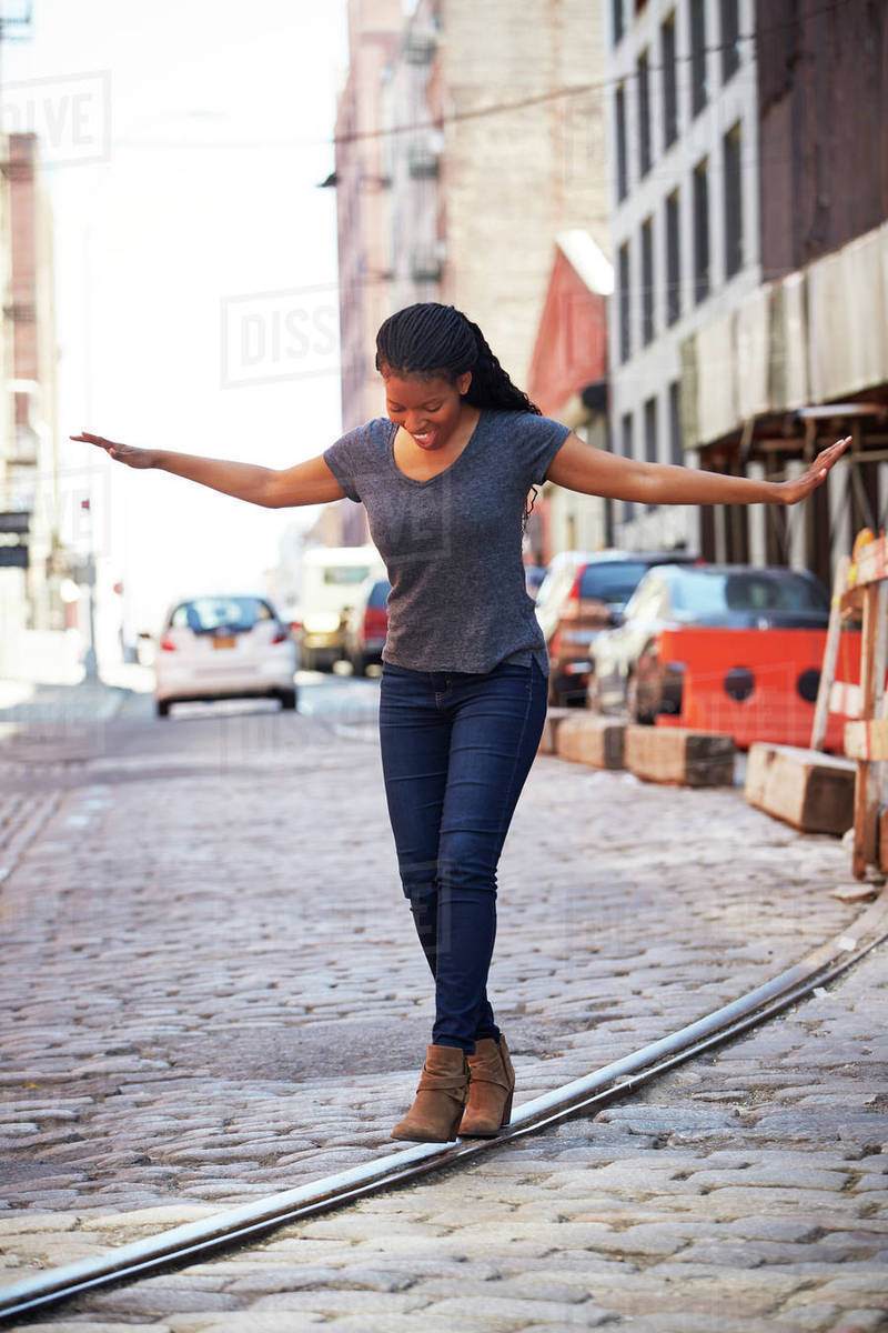 Black woman balancing on track in cobblestone city street - Royalty ...