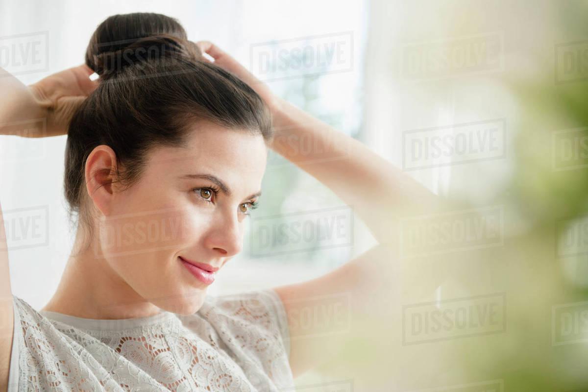 Caucasian woman tying hair in bun - Stock Photo - Dissolve