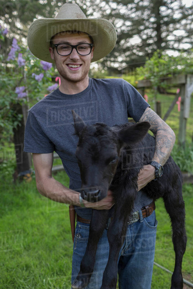 Caucasian farmer carrying calf - Stock Photo - Dissolve