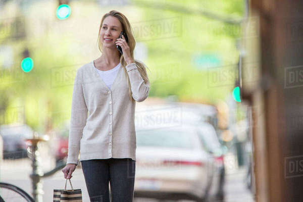 Caucasian woman carrying shopping bag using cell phone - Royalty-free ...