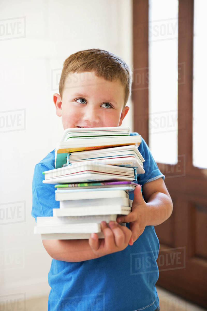 Caucasian boy carrying stack of books - Stock Photo - Dissolve
