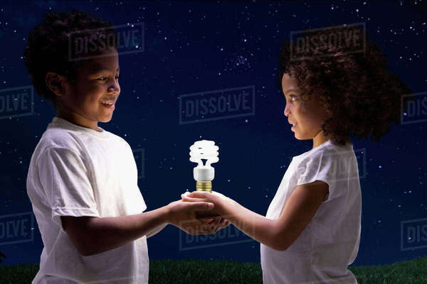 African children holding glowing cfl lightbulb - Stock Photo - Dissolve