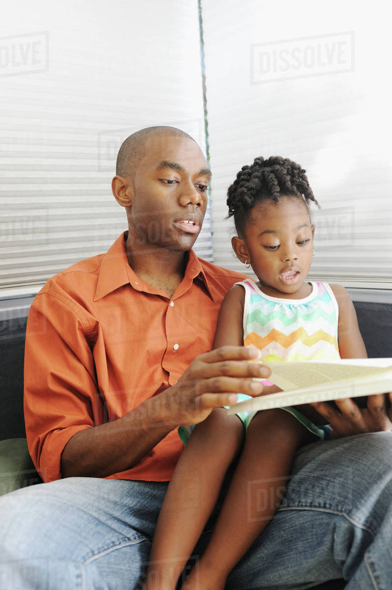 Black father reading book to daughter - Royalty-free Stock Photo | Dissolve