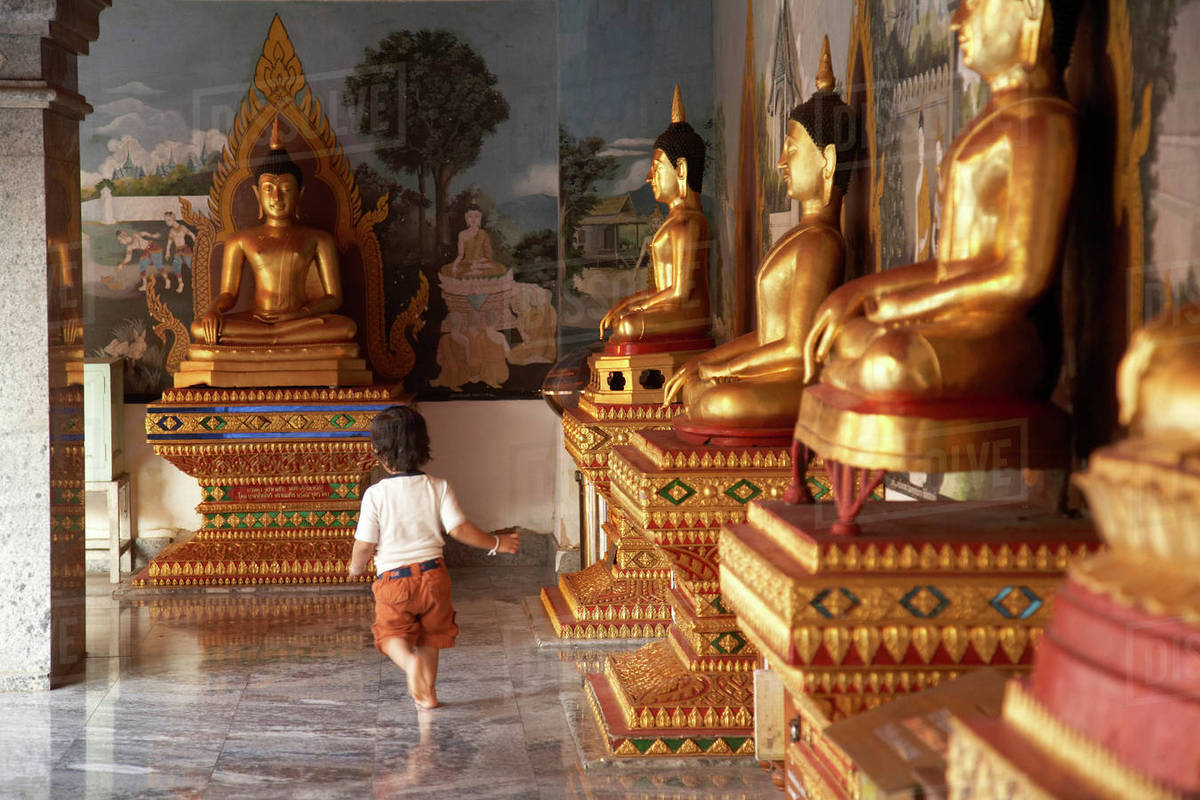 Mixed race child running past Buddha statues - Stock Photo - Dissolve