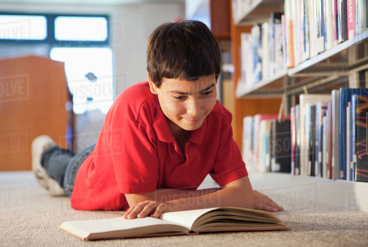 Hispanic boy reading book in library - Royalty-free Stock Photo | Dissolve