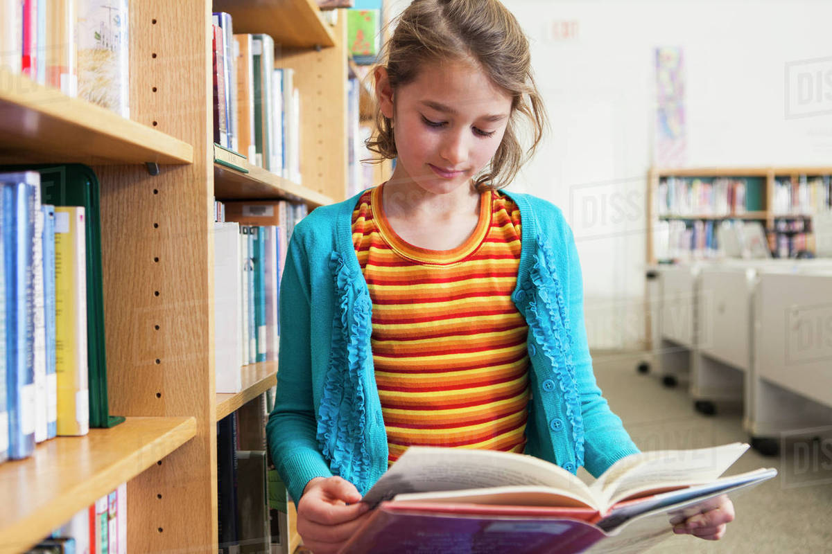Caucasian girl reading book in library - Stock Photo - Dissolve