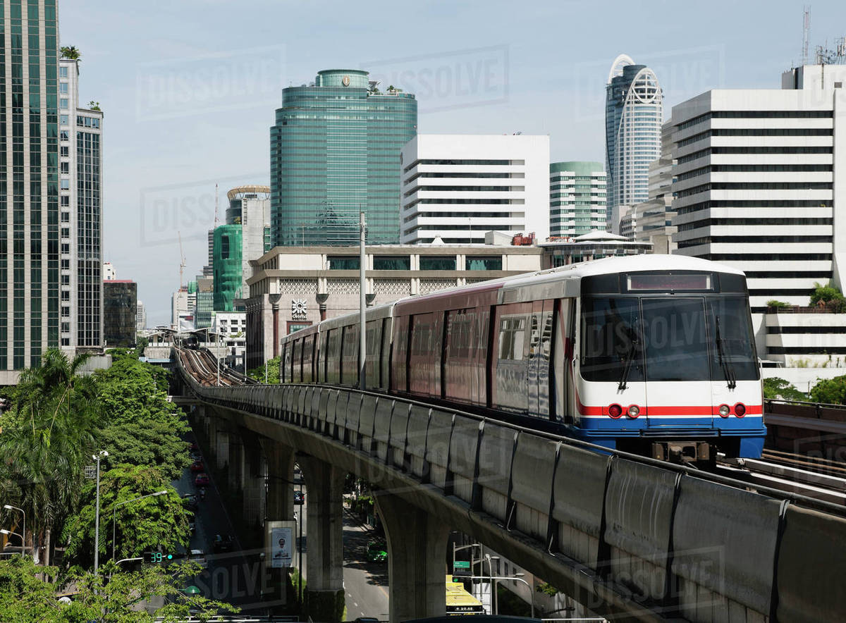 A mass transit train on an elevated track passes modern building ...