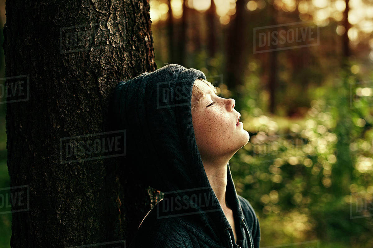 Caucasian boy leaning against tree - Royalty-free Stock Photo | Dissolve