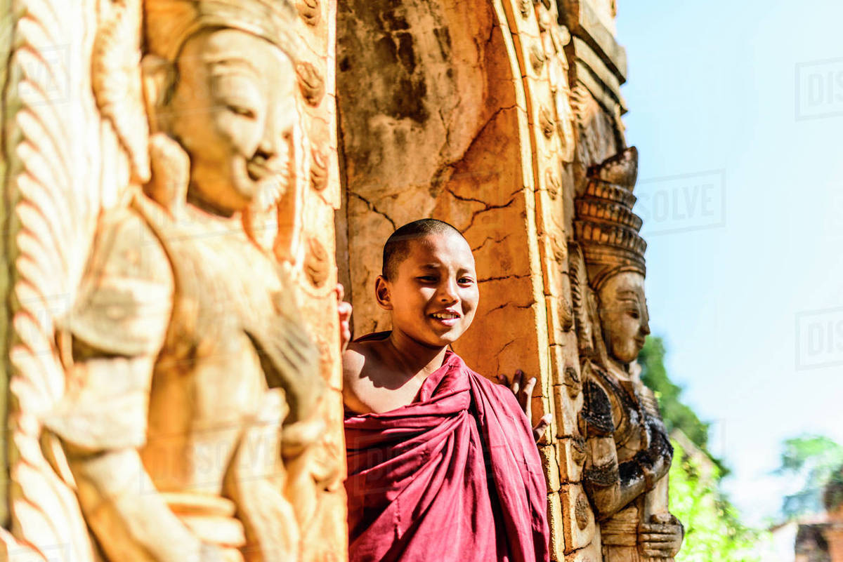 Asian monk-in-training peering around carved temple walls - Royalty ...