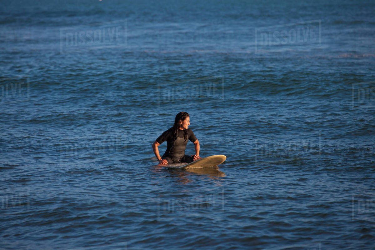 Hispanic surfer floating on surfboard in ocean - Stock Photo - Dissolve