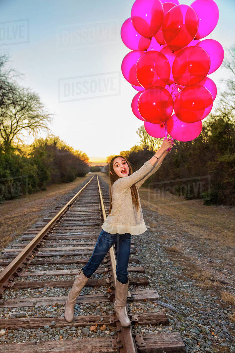 Caucasian teenage girl holding bunch of balloons on train tracks ...