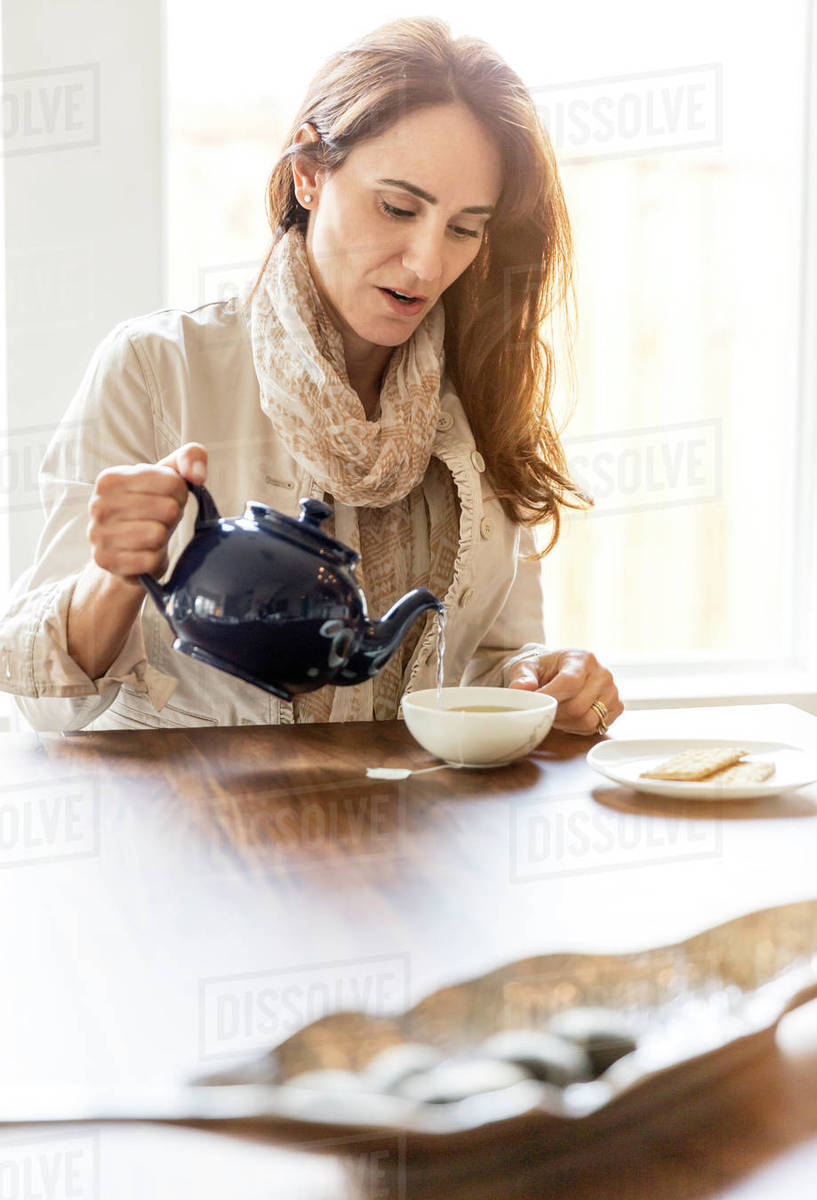 Caucasian woman pouring cup of tea at table - Stock Photo - Dissolve
