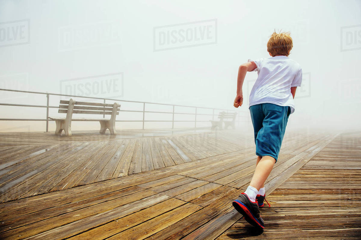 Caucasian boy running on wooden boardwalk - Stock Photo - Dissolve