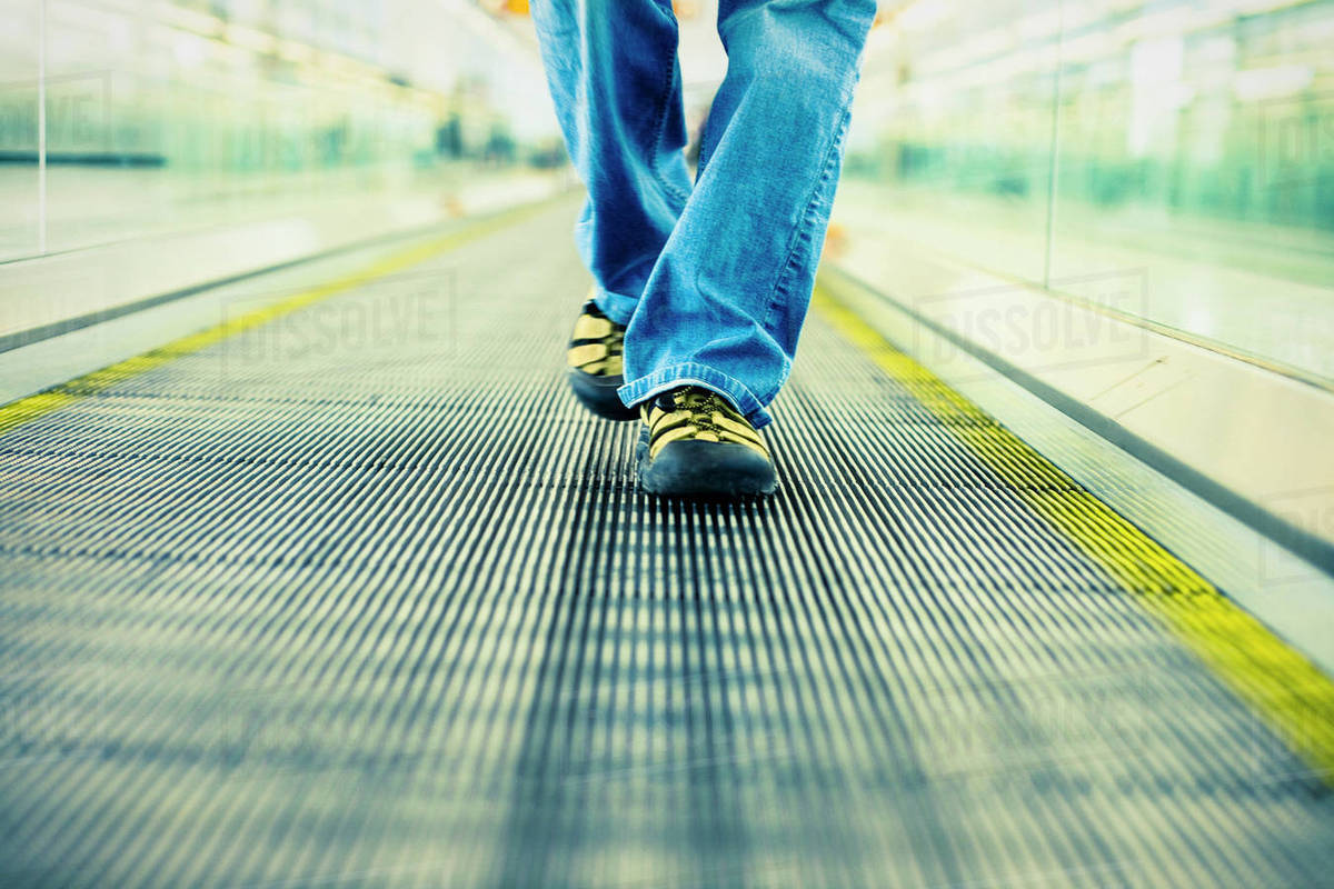 Legs of Japanese woman wearing jeans walking on moving walkway ...