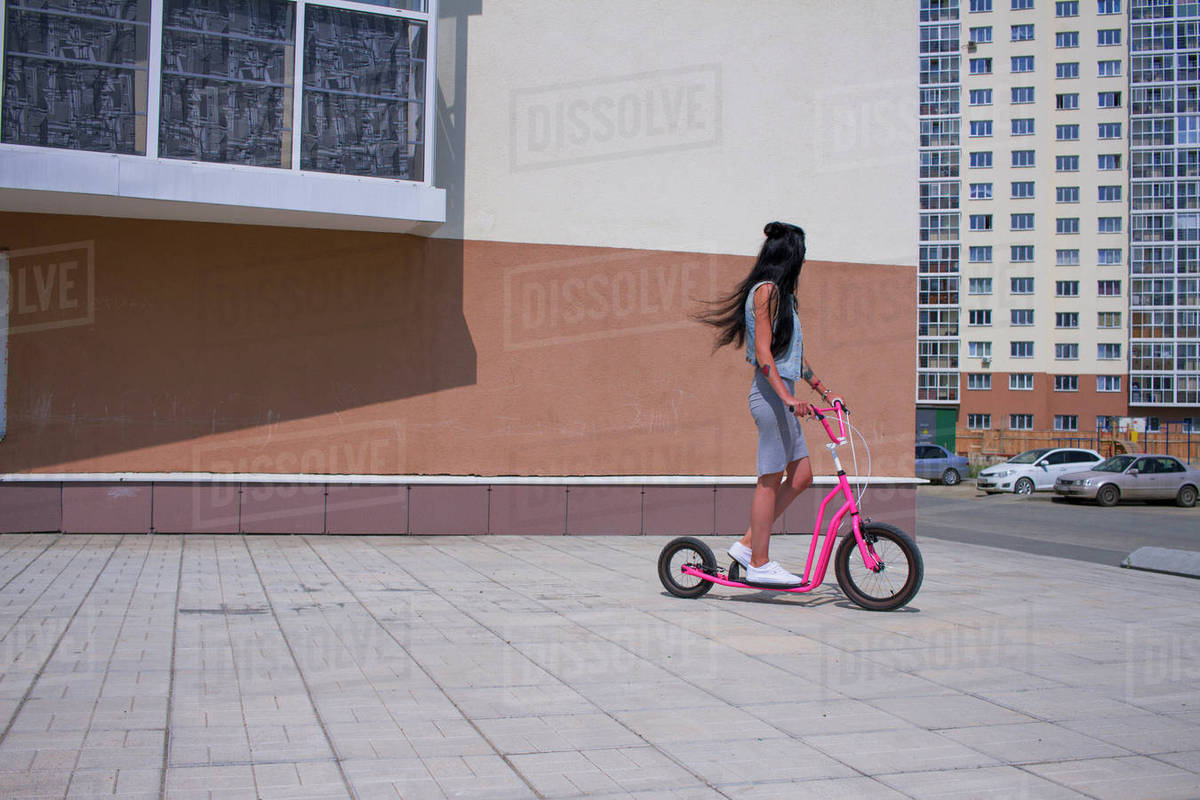 Caucasian woman riding push scooter on city sidewalk - Royalty-free ...