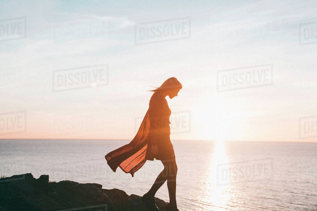 Silhouette of Caucasian woman walking on rocks at ocean - Royalty-free ...