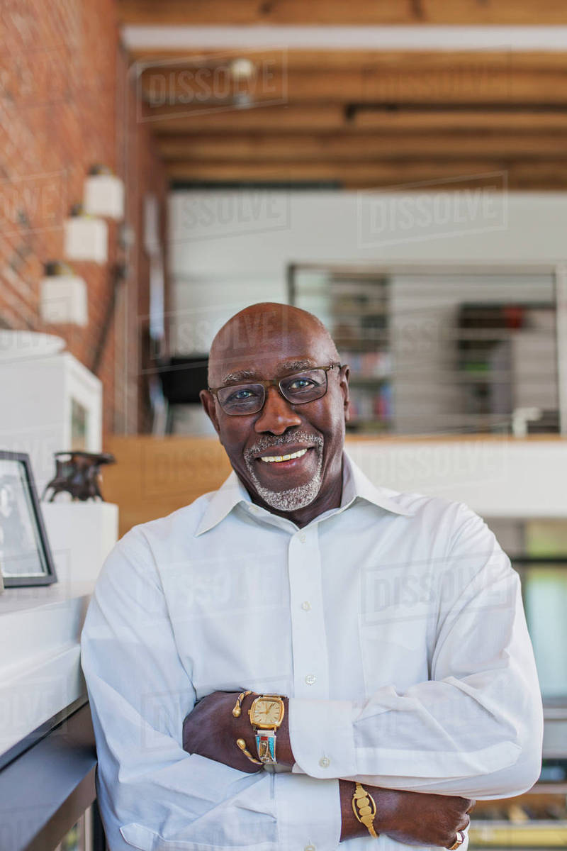 Smiling man with arms crossed leaning on mantle - Stock Photo - Dissolve