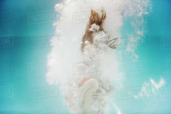 Caucasian girl swimming underwater holding nose - Stock Photo - Dissolve