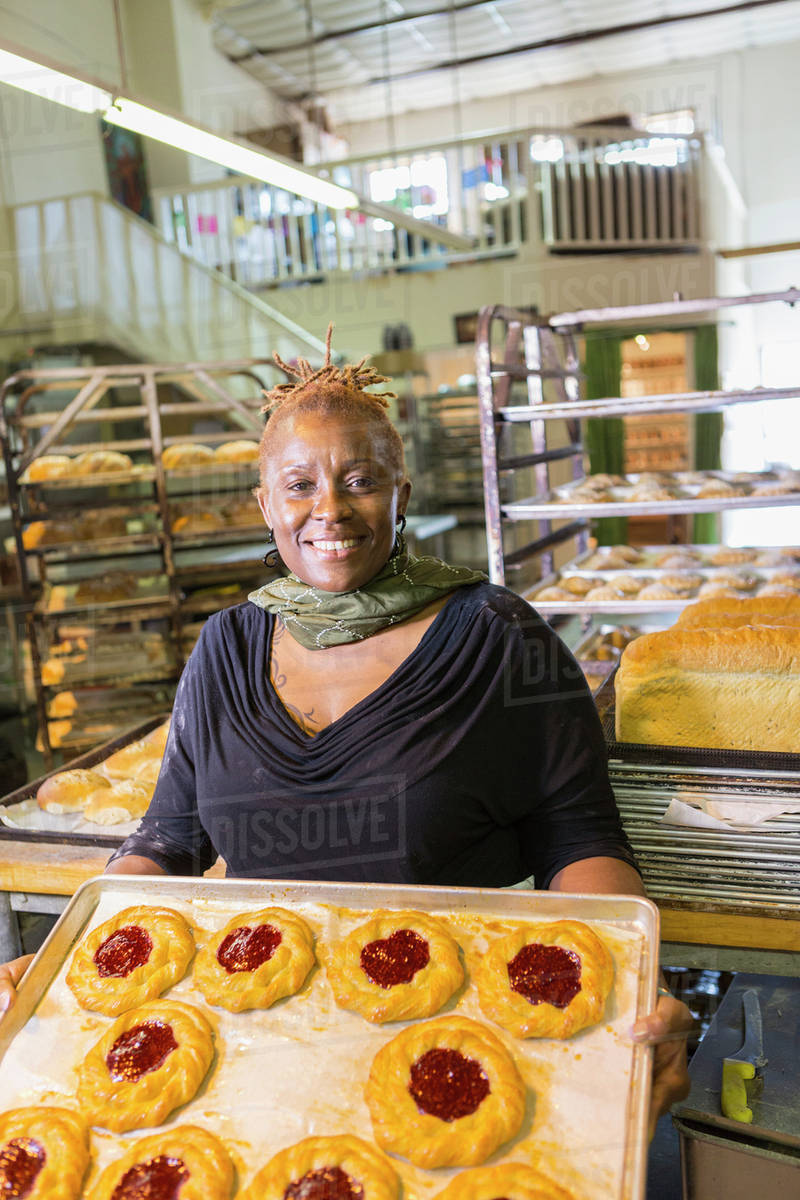 Black baker holding tray of pastries in bakery kitchen - Stock Photo ...