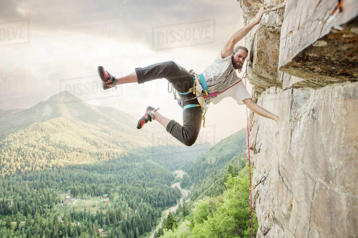Man hanging from rock while climbing - Stock Photo - Dissolve