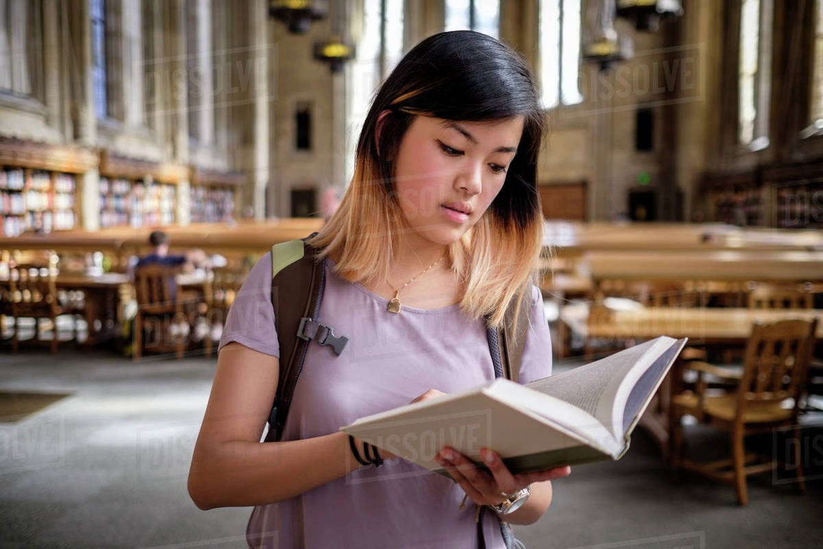 Chinese woman standing in library reading book - Royalty-free Stock ...