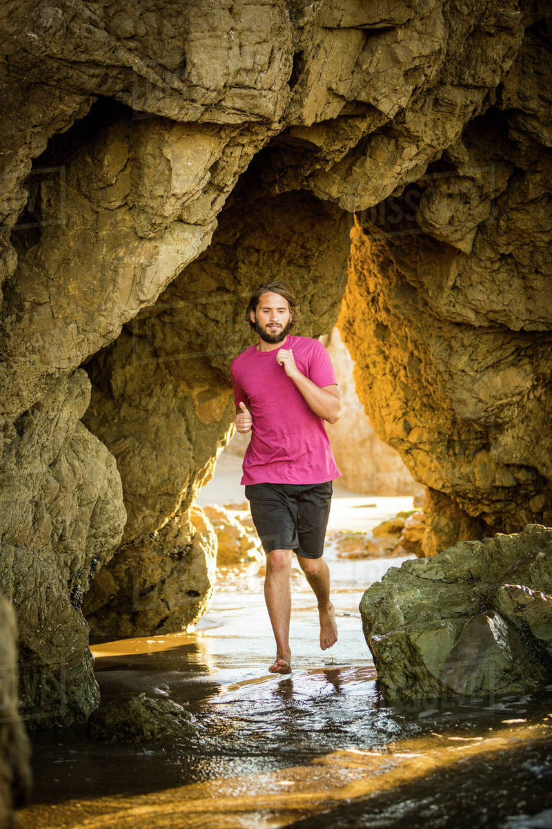 Caucasian man running under rock formation at beach - Royalty-free ...