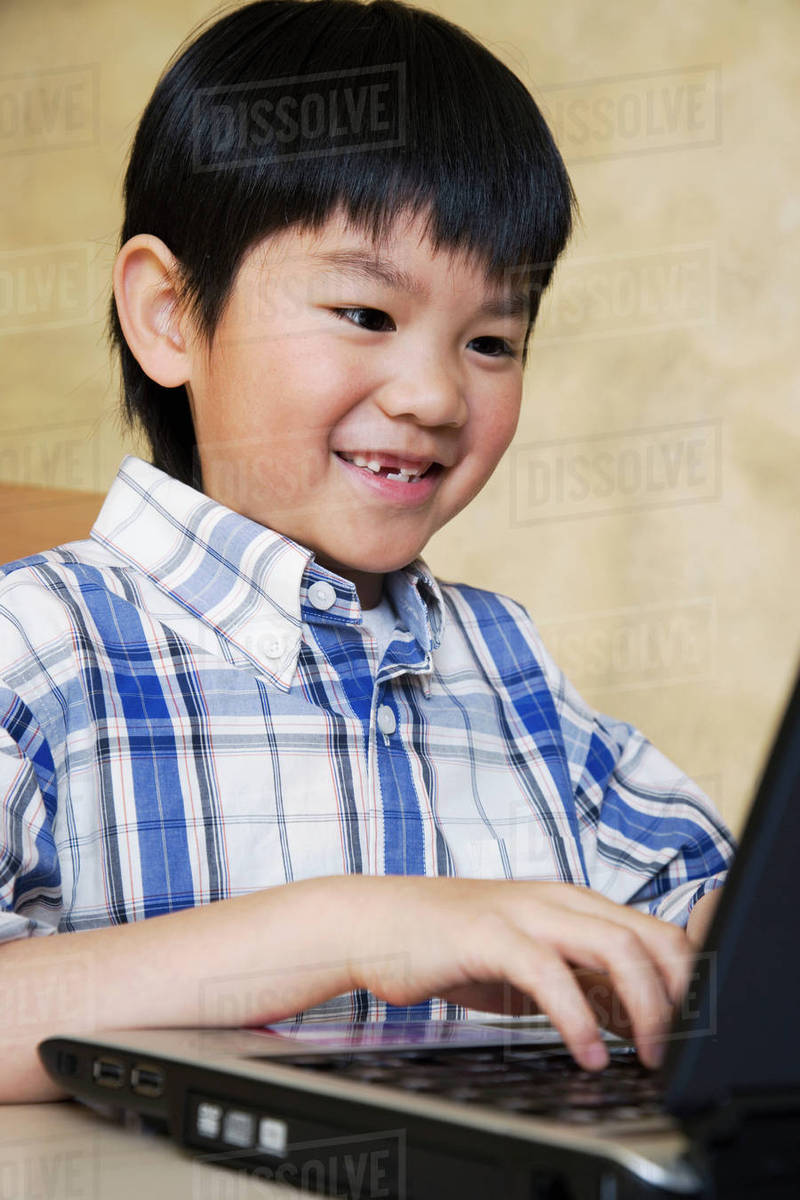 Asian boy typing on laptop - Stock Photo - Dissolve