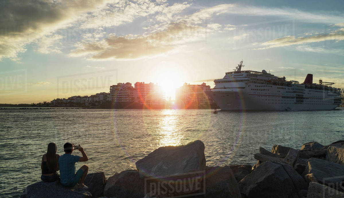Couple sitting on rocks at river watching sunset - Stock Photo - Dissolve