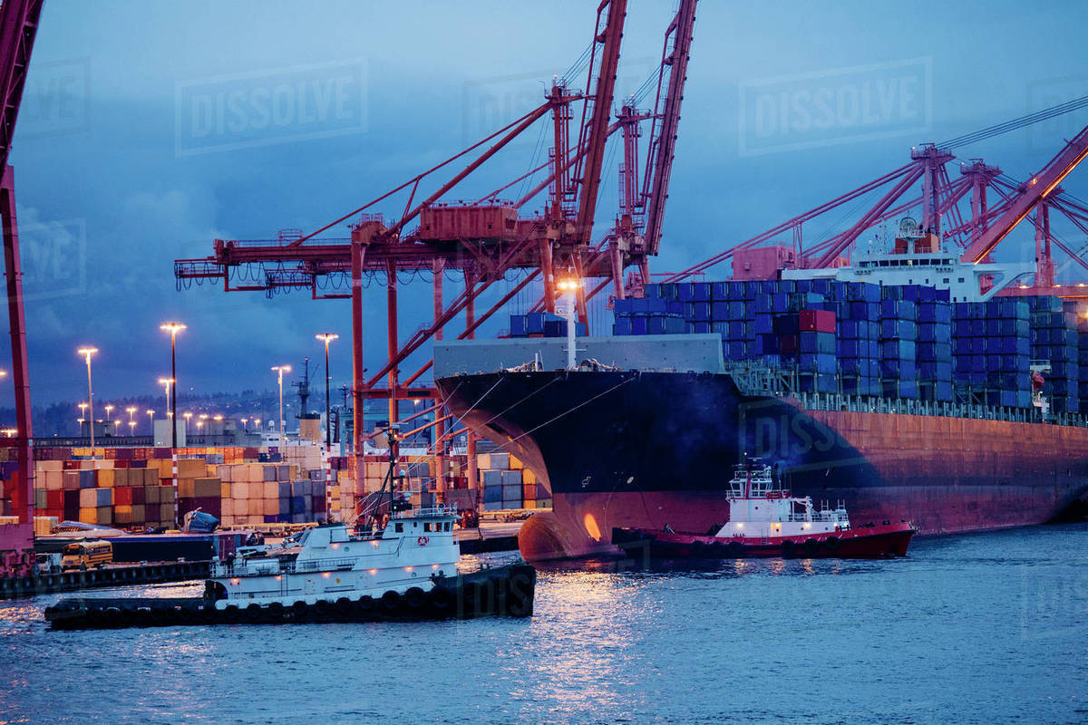 Cargo containers on freighter at shipping port near tugboats - Royalty ...