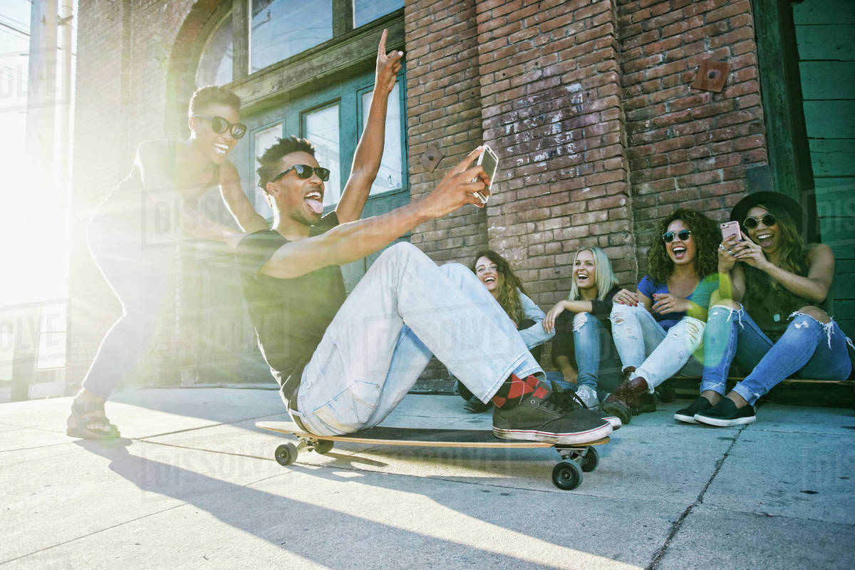 Woman pushing friend sitting on skateboard in city - Stock Photo - Dissolve