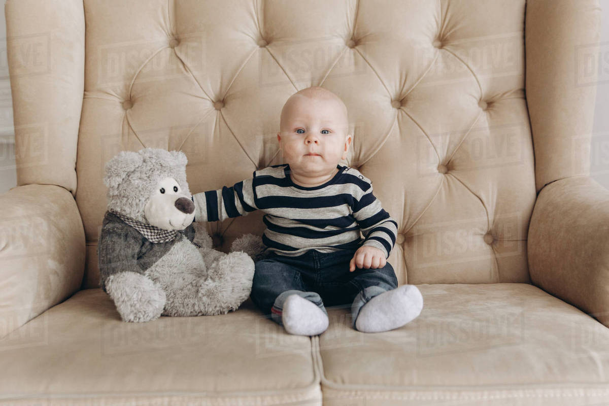 Portrait of Caucasian baby boy sitting on love seat with teddy bear ...