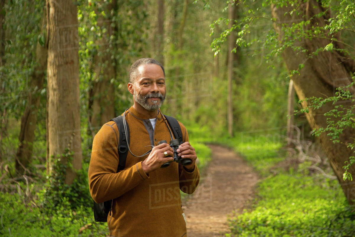 African American man standing on path in forest holding binoculars ...