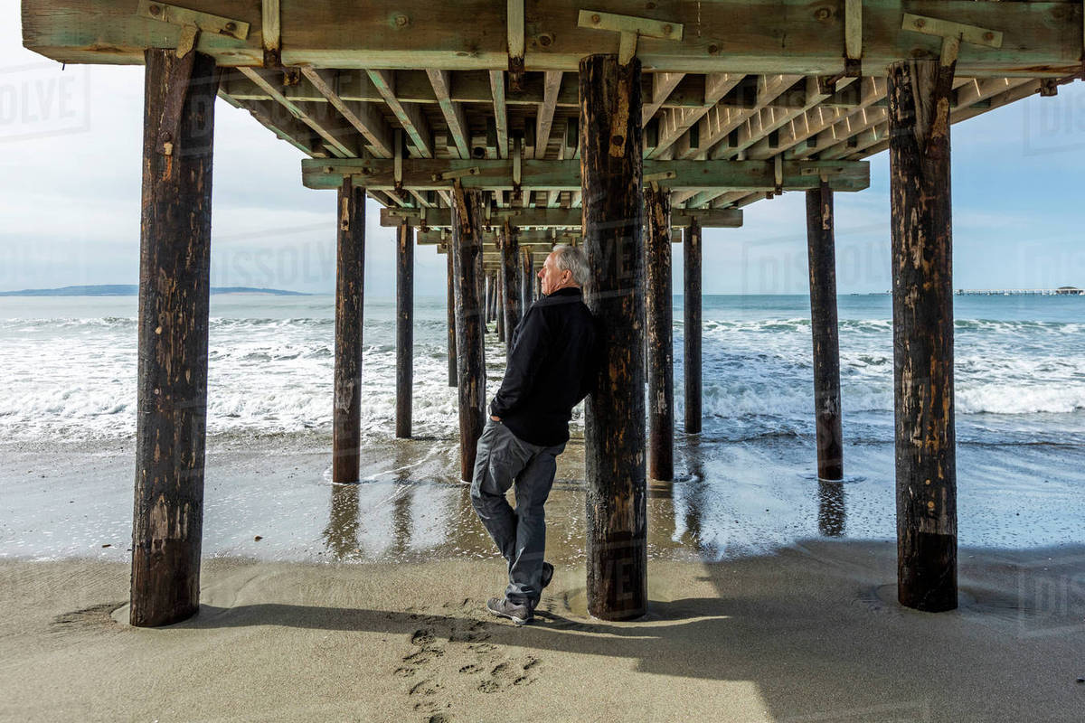 Caucasian man leaning on piling of wooden pier at beach - Royalty-free ...