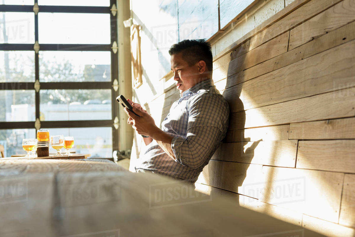 Asian man texting on cell phone in brew pub - Stock Photo - Dissolve