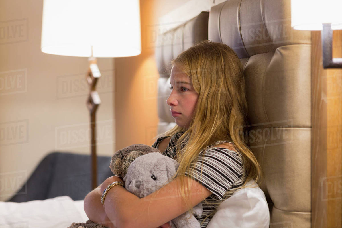 Frustrated Caucasian girl holding stuffed animals on hotel bed ...