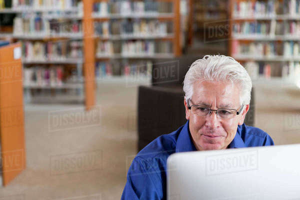 Smiling Hispanic man using computer in library - Stock Photo - Dissolve