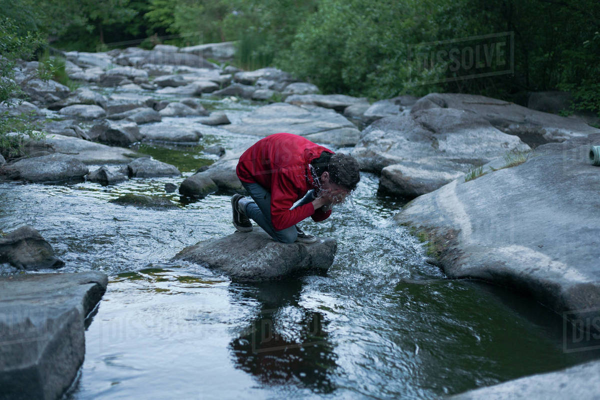 Caucasian man kneeling on rock in river splashing water on face - Stock ...