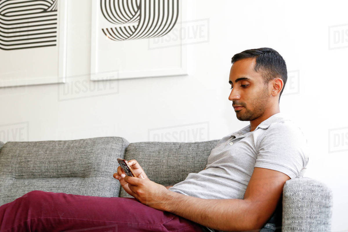 Mixed race man sitting on sofa texting on cell phone - Royalty-free ...