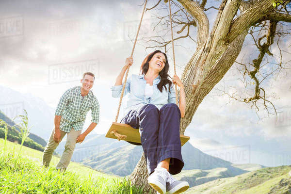 Man pushing woman swinging on tree swing - Royalty-free Stock Photo ...