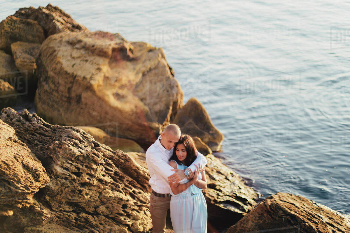 Caucasian couple hugging on rocks on beach - Royalty-free Stock Photo ...