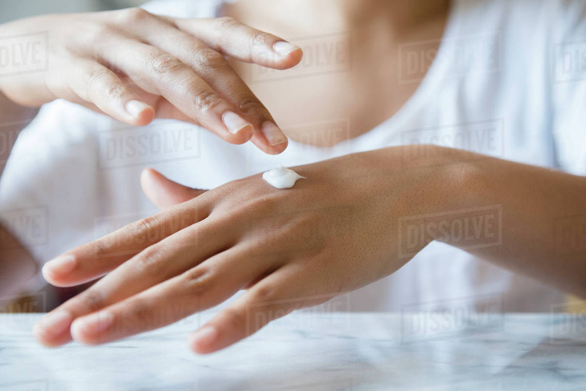 African American woman applying lotion to hand - Stock Photo - Dissolve