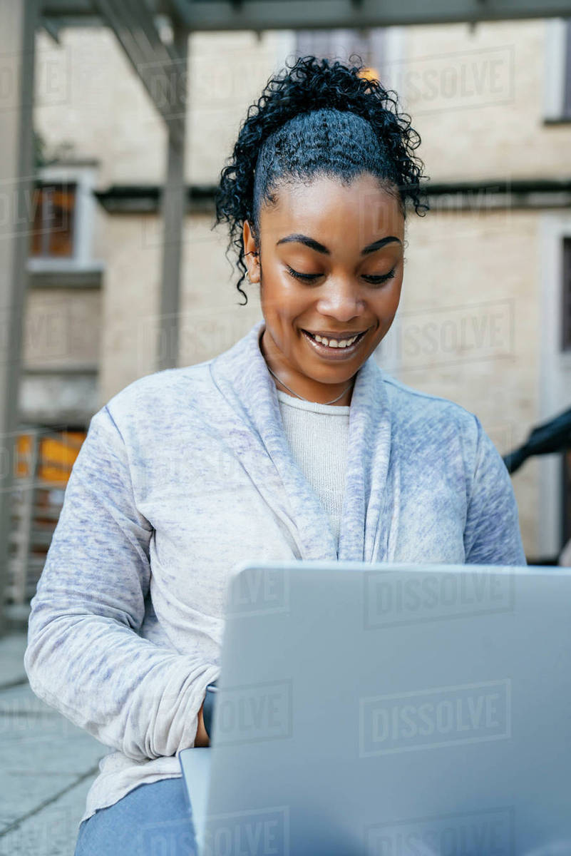 Smiling Black woman using laptop outdoors - Stock Photo - Dissolve