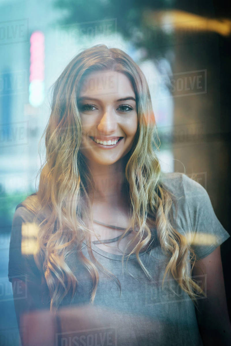 Portrait of smiling Caucasian woman behind window - Stock Photo - Dissolve