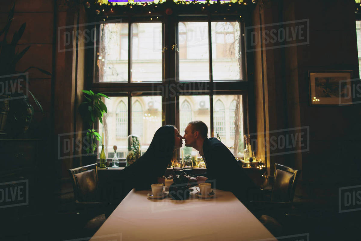Caucasian couple sitting at table rubbing noses - Stock Photo - Dissolve
