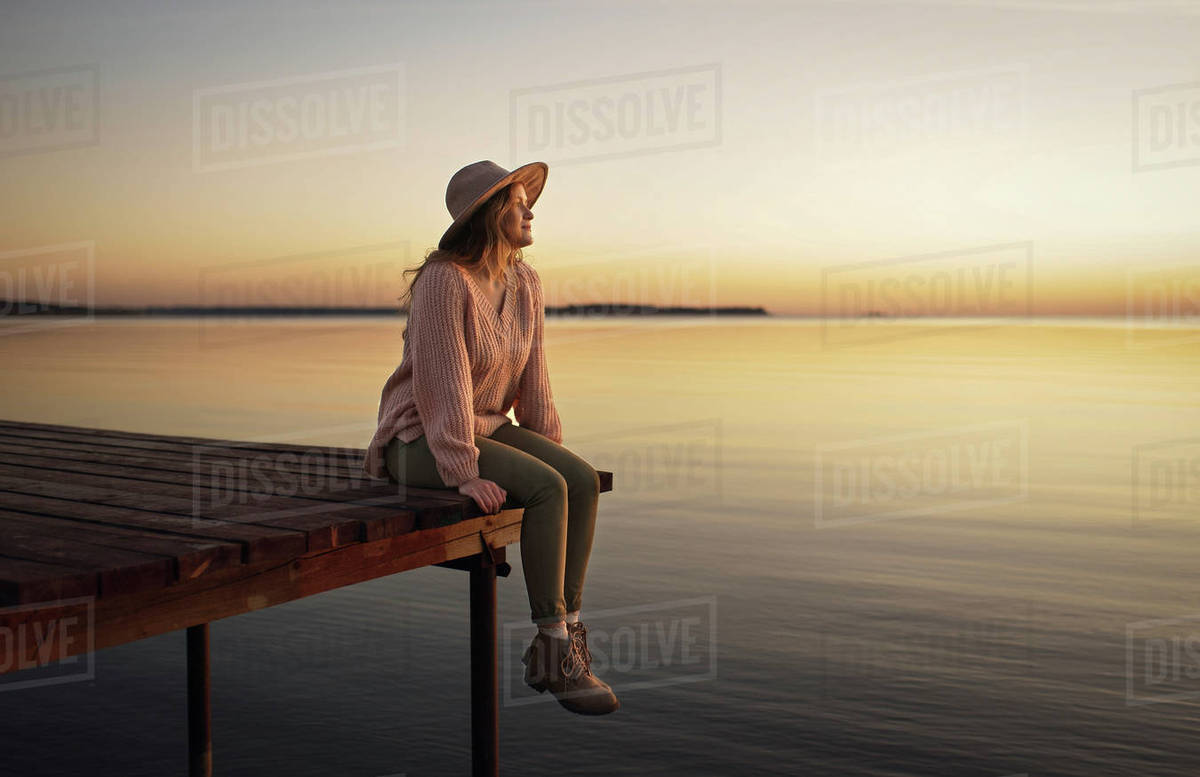 Caucasian woman sitting on dock of lake admiring sunset - Royalty-free ...